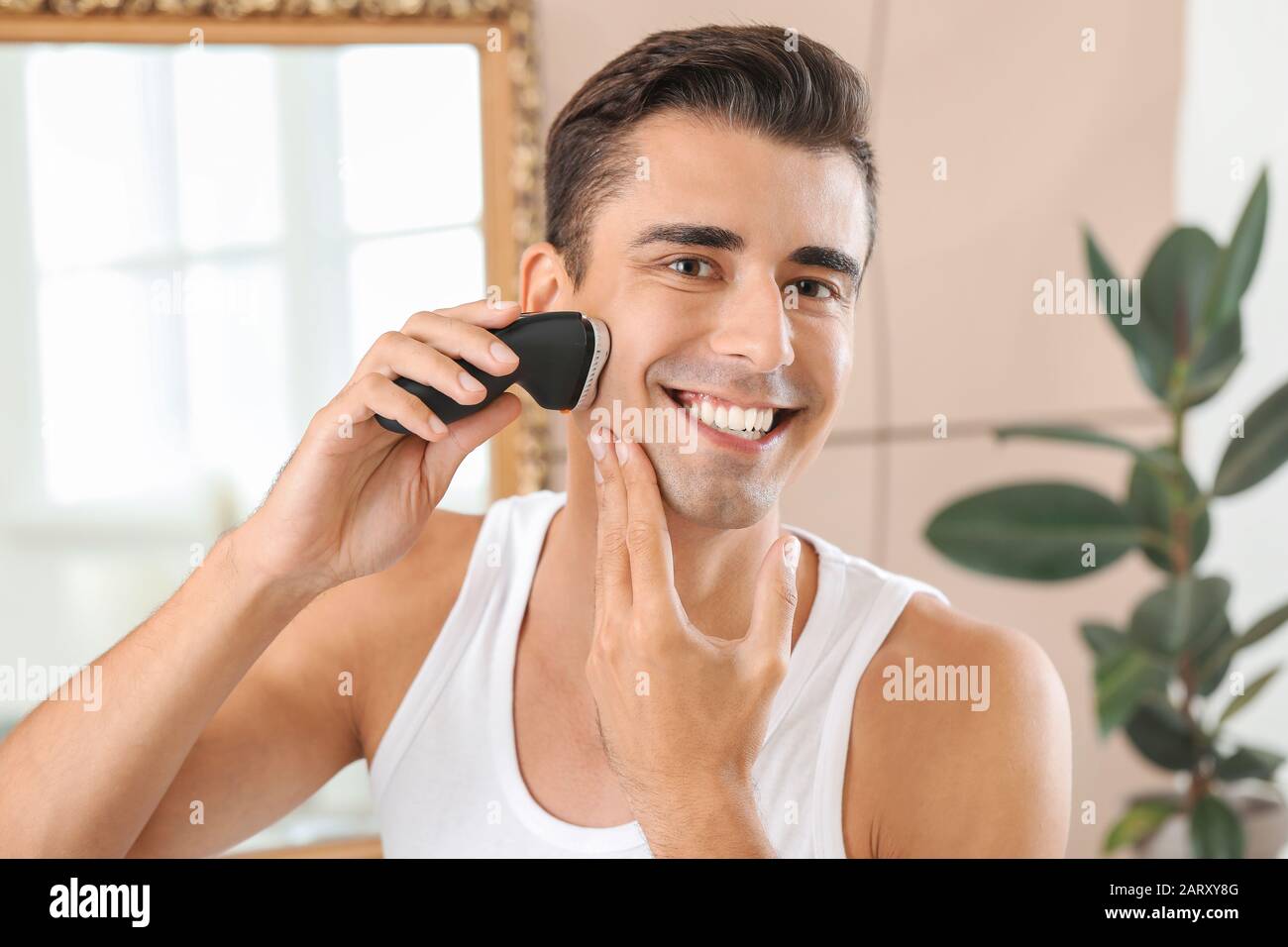 Handsome young man shaving in bathroom Stock Photo - Alamy