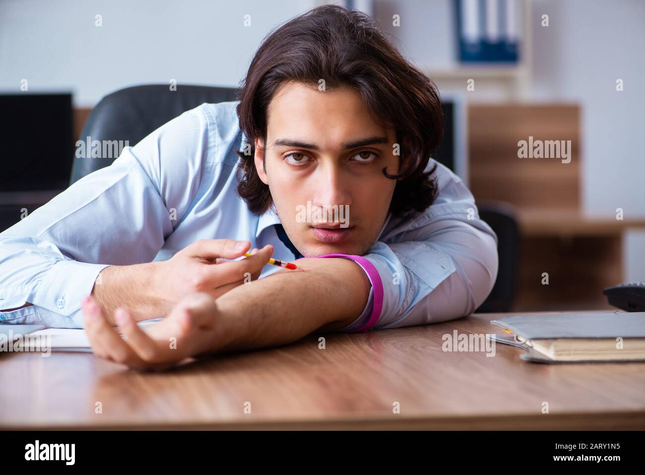 The young man having problems with narcotics at workplace Stock Photo ...