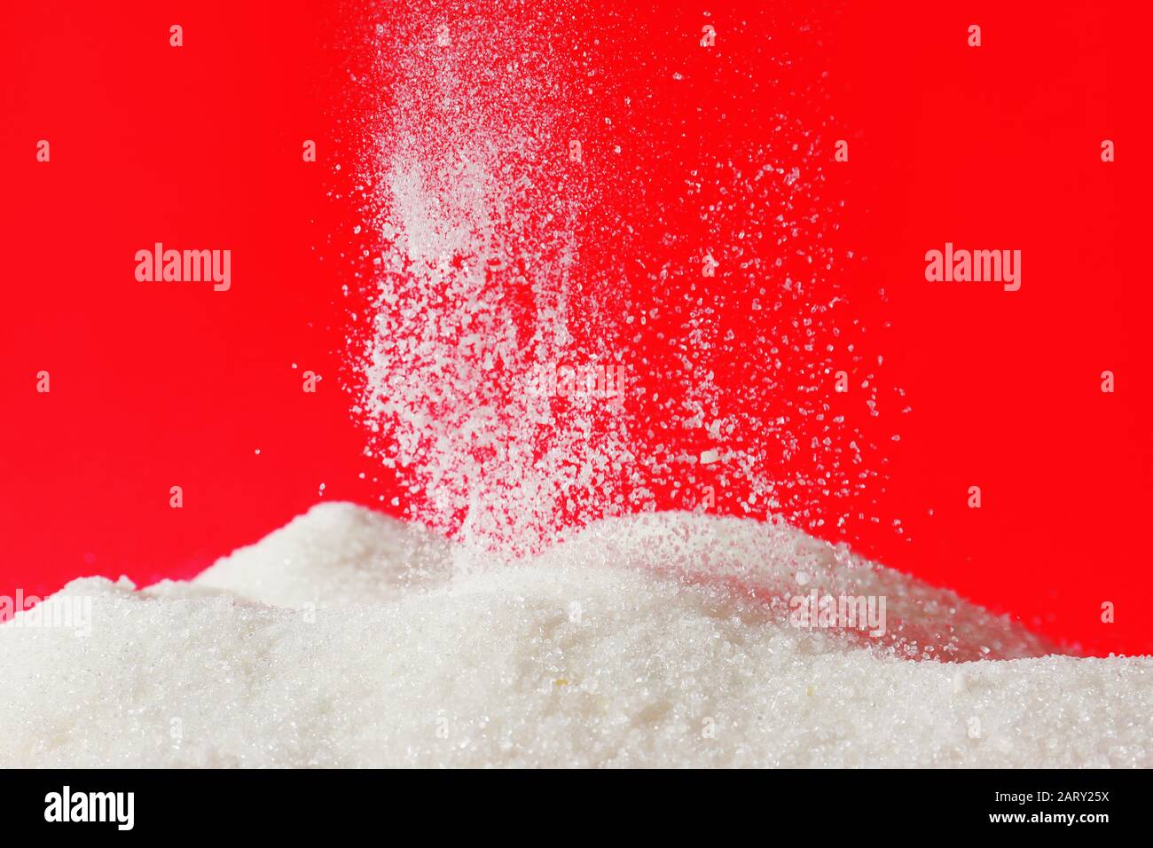 Pouring of sugar against color background Stock Photo - Alamy