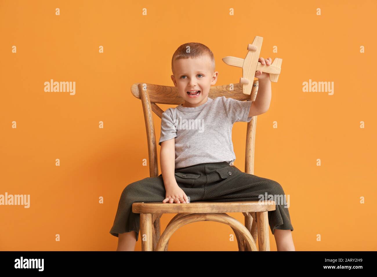 Portrait of cute little boy with toy sitting on chair against color ...