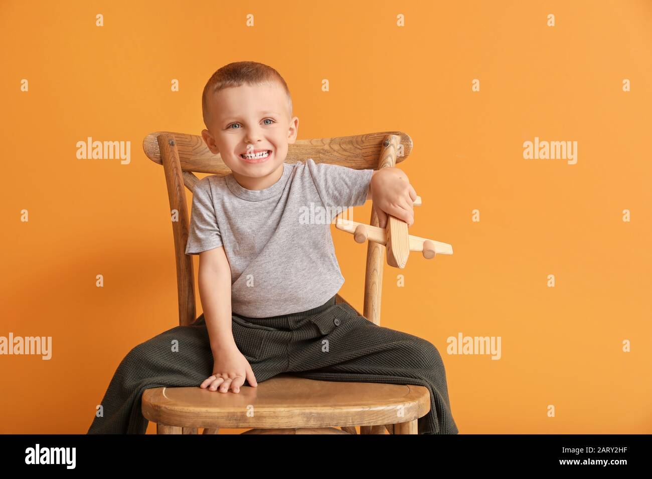 Portrait of cute little boy with toy sitting on chair against color ...