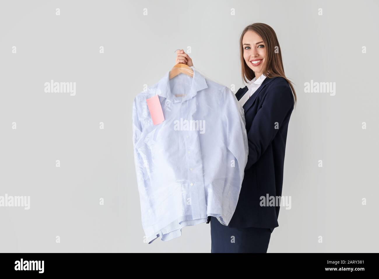 Female worker of modern dry-cleaner's with clothes on light background ...
