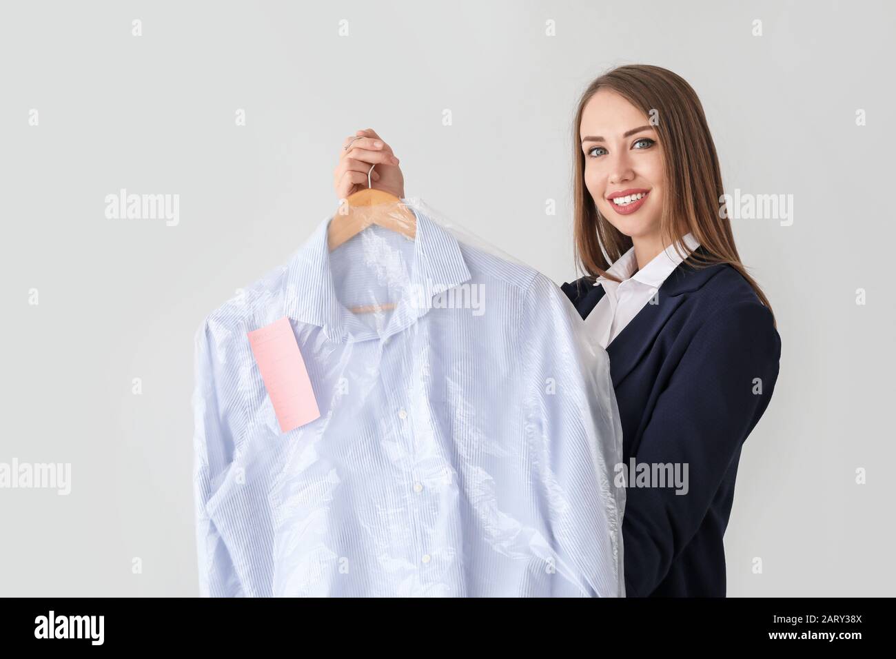 Female worker of modern dry-cleaner's with clothes on light background ...