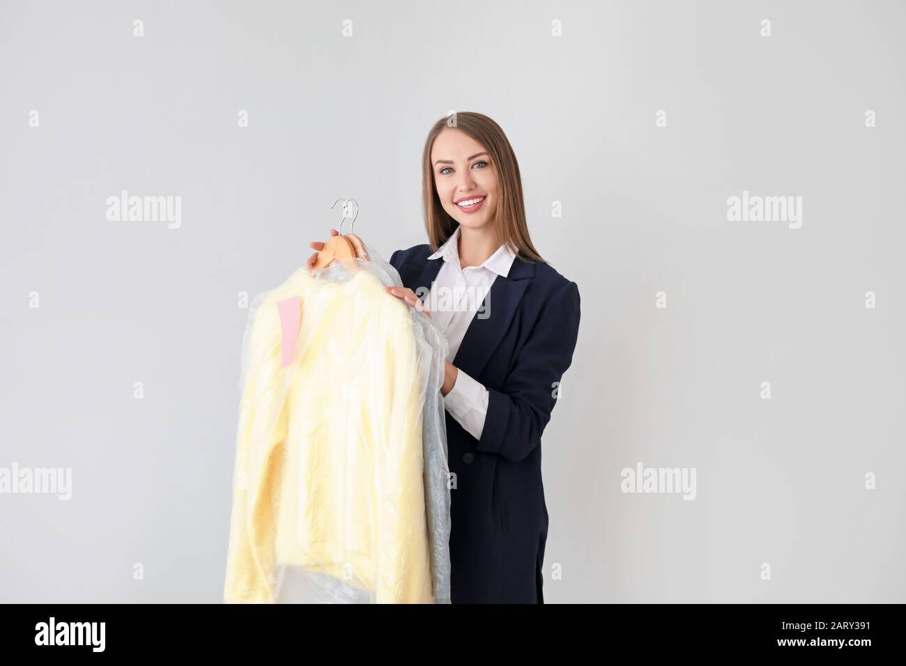Female worker of modern dry-cleaner's with clothes on light background ...