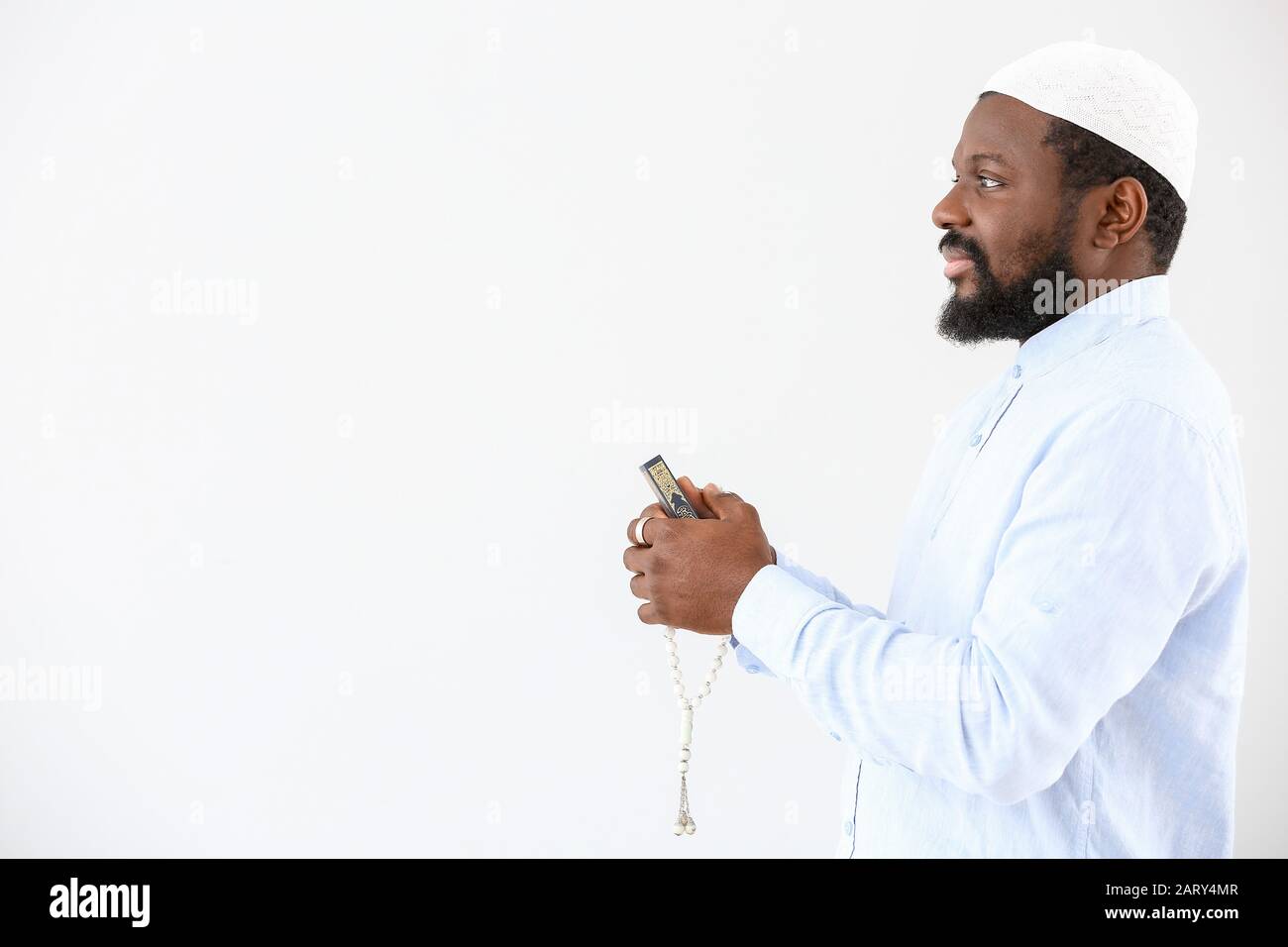 African-American Muslim man with Koran and beads on light background ...