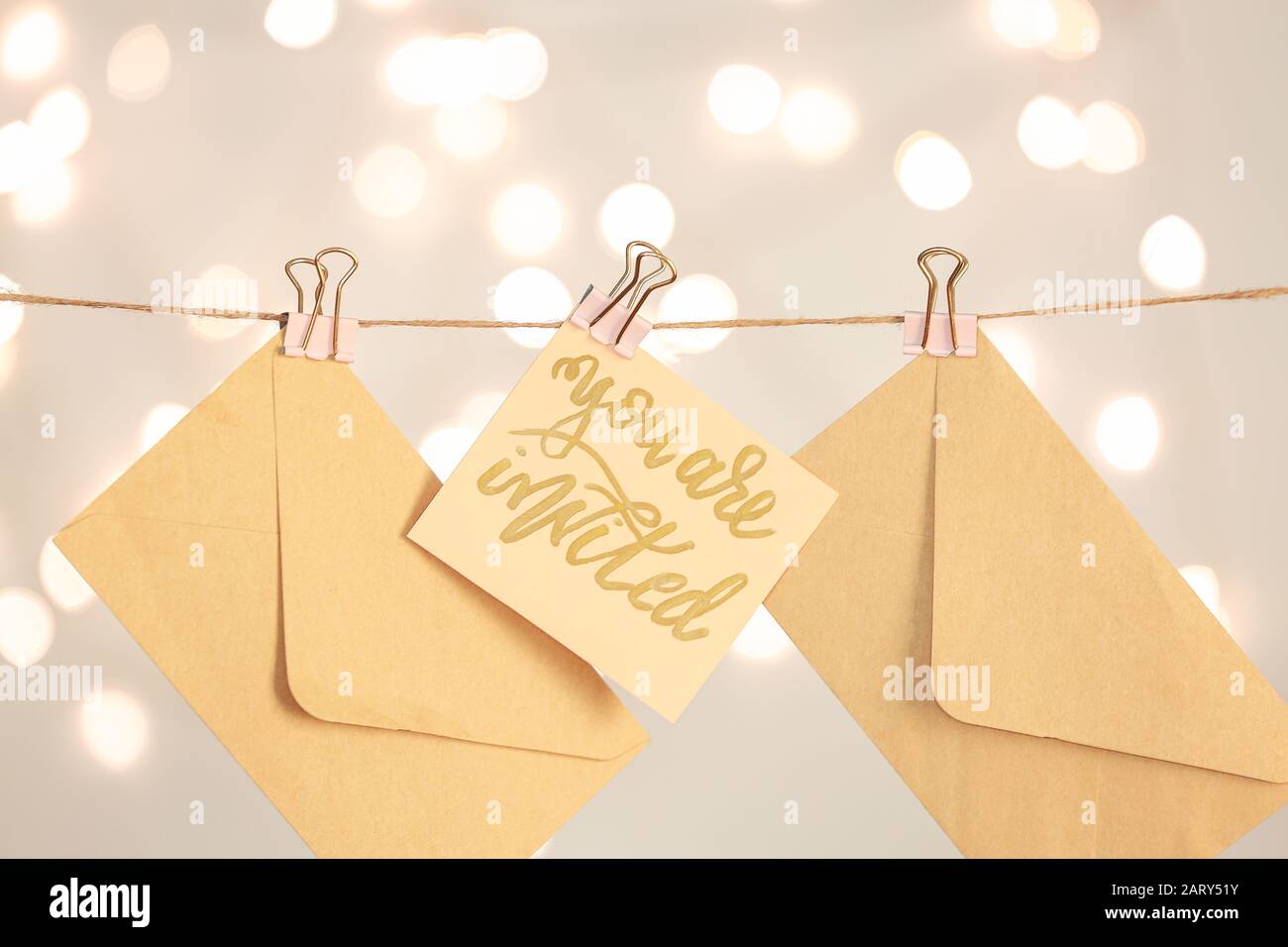 Invitation with envelopes hanging on rope against light background ...
