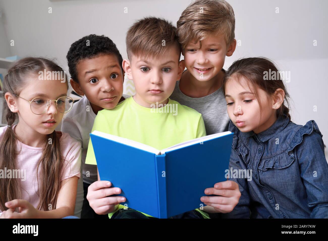 Surprised little children reading book indoors Stock Photo - Alamy