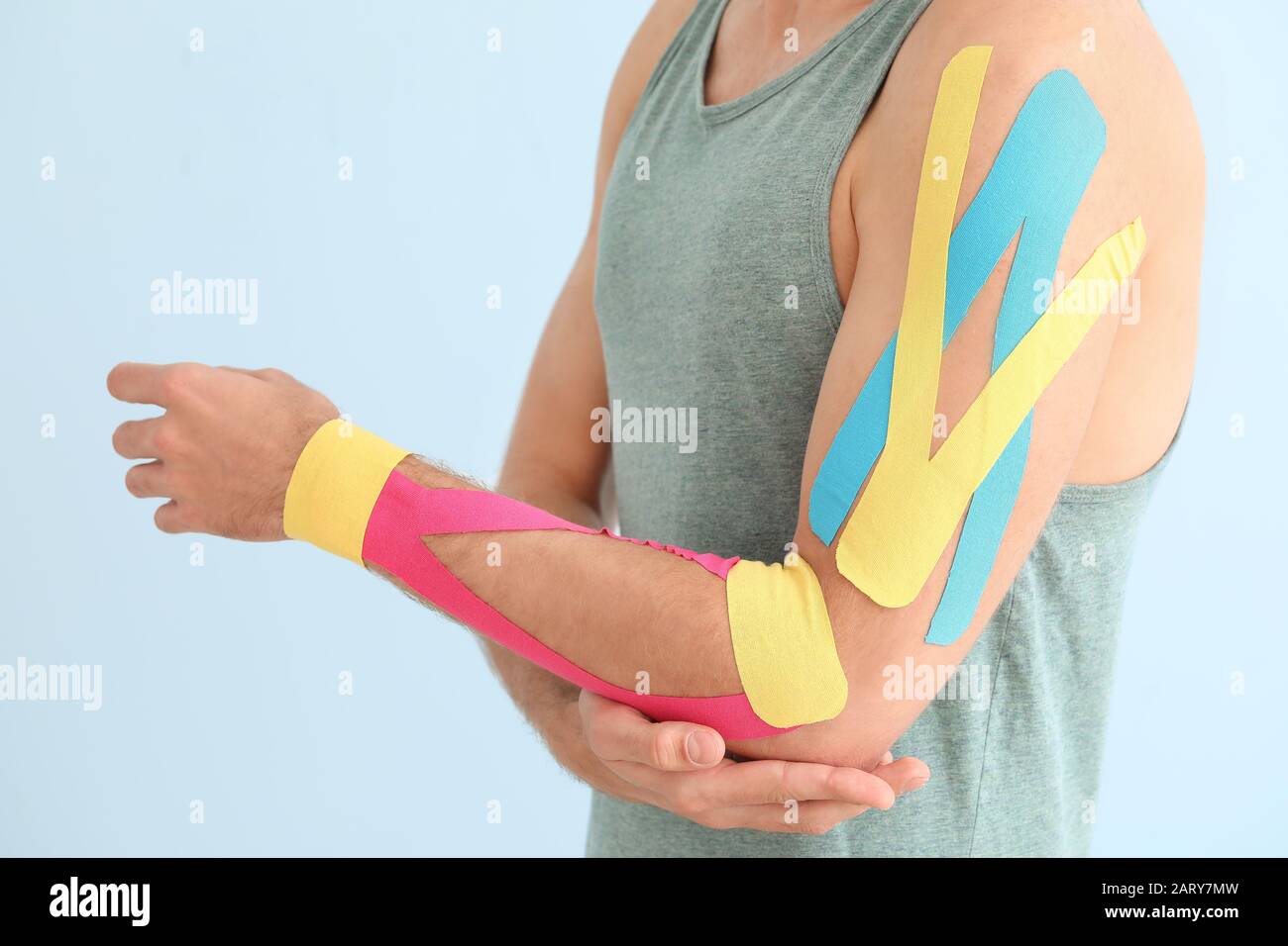 Sporty man with physio tape applied on arm against light background ...