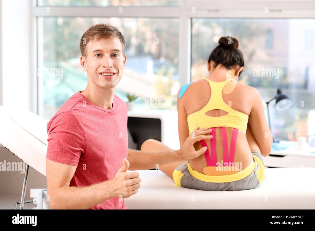 Physiotherapist applying tape onto woman's lower back in clinic Stock ...