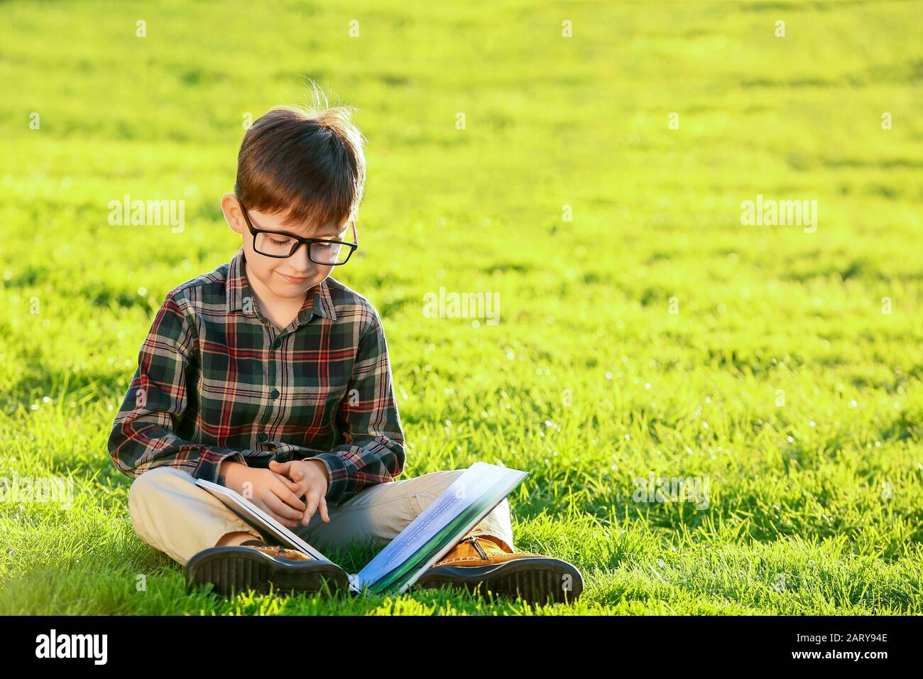 Cute little boy reading book outdoors Stock Photo - Alamy