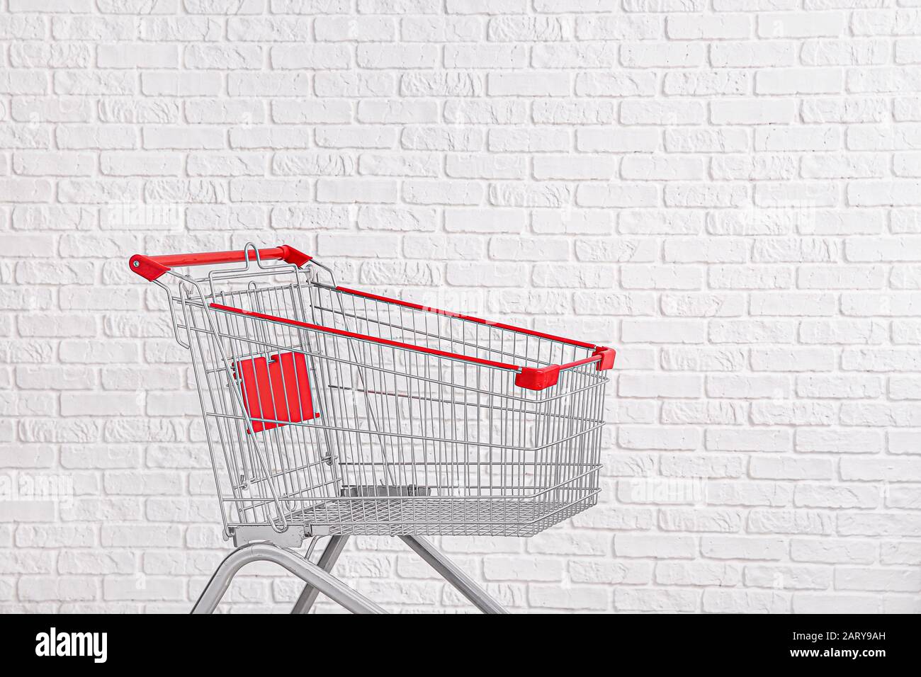 Empty shopping cart near light brick wall Stock Photo - Alamy