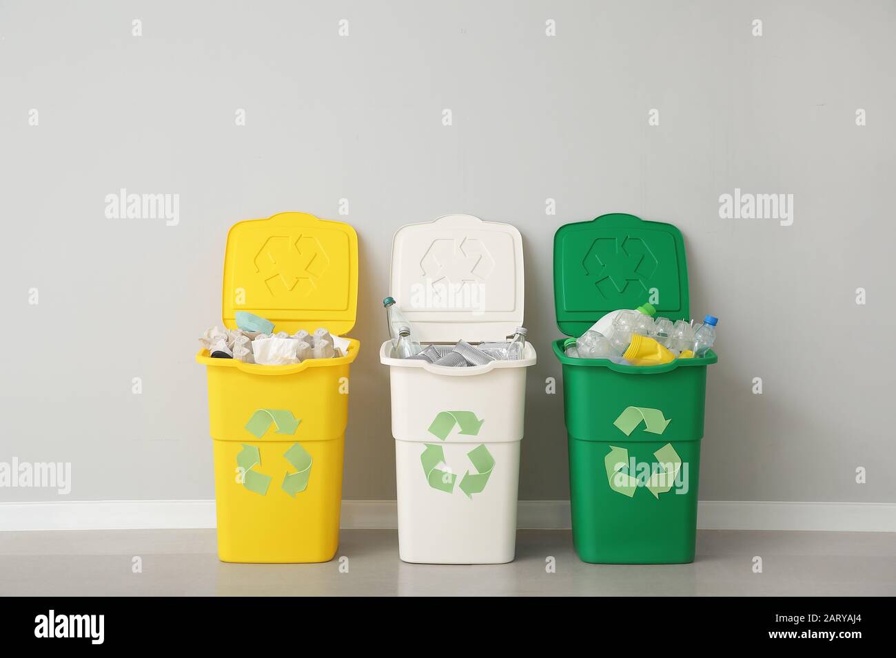 Containers with different types of garbage near light wall. Recycling ...