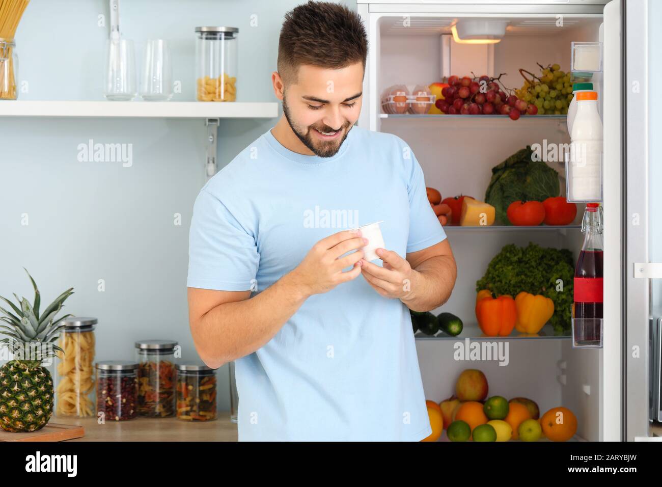 Young man taking food out of fridge in kitchen Stock Photo - Alamy