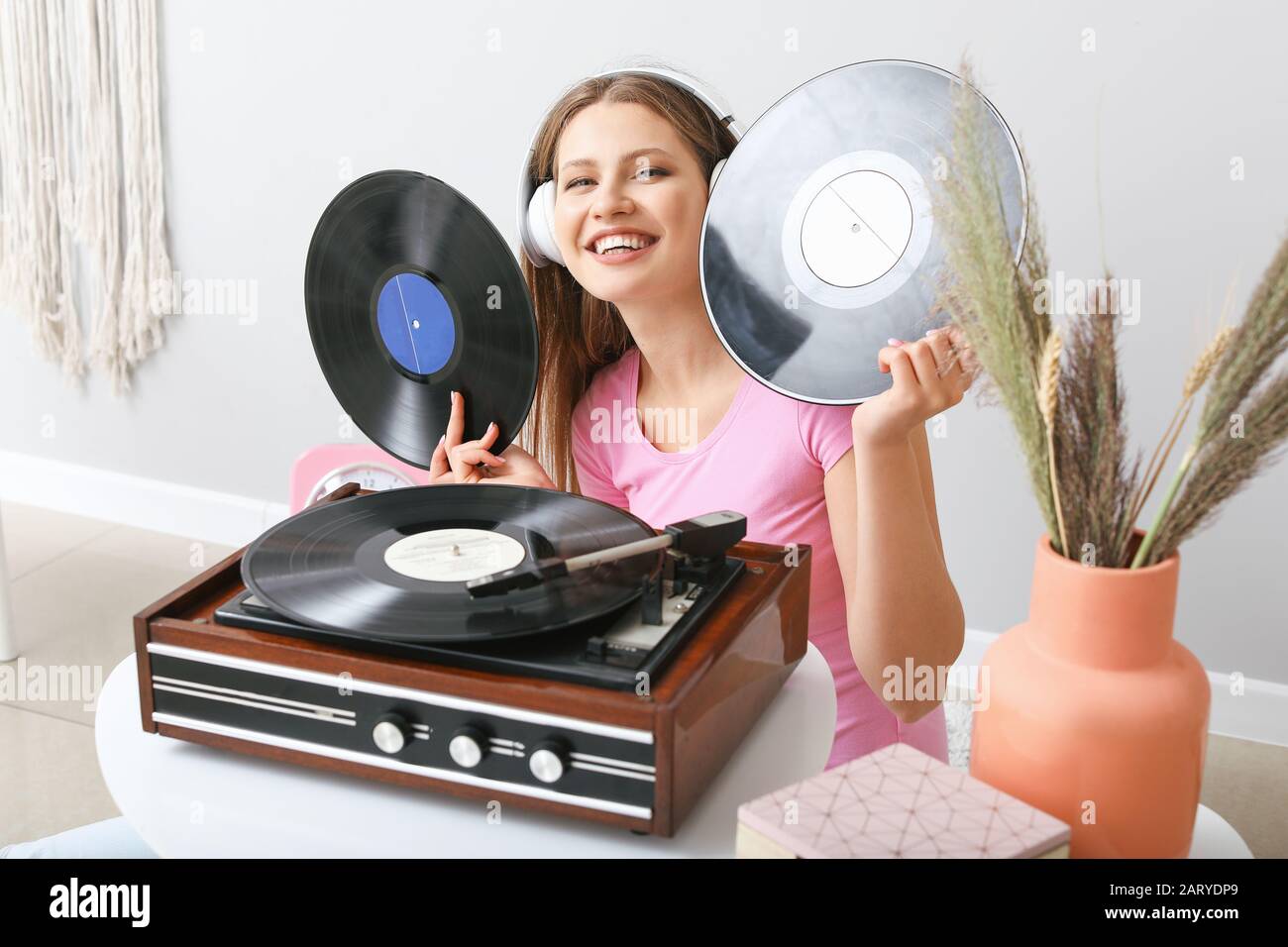 Beautiful young woman listening to music through record player at home ...