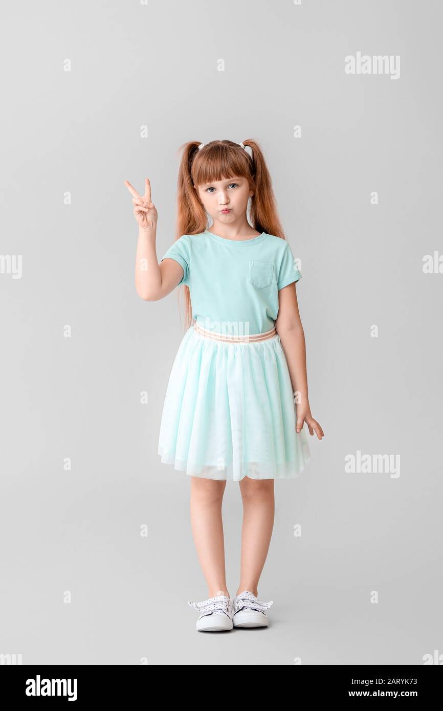 Cute little girl showing victory gesture on light background Stock ...
