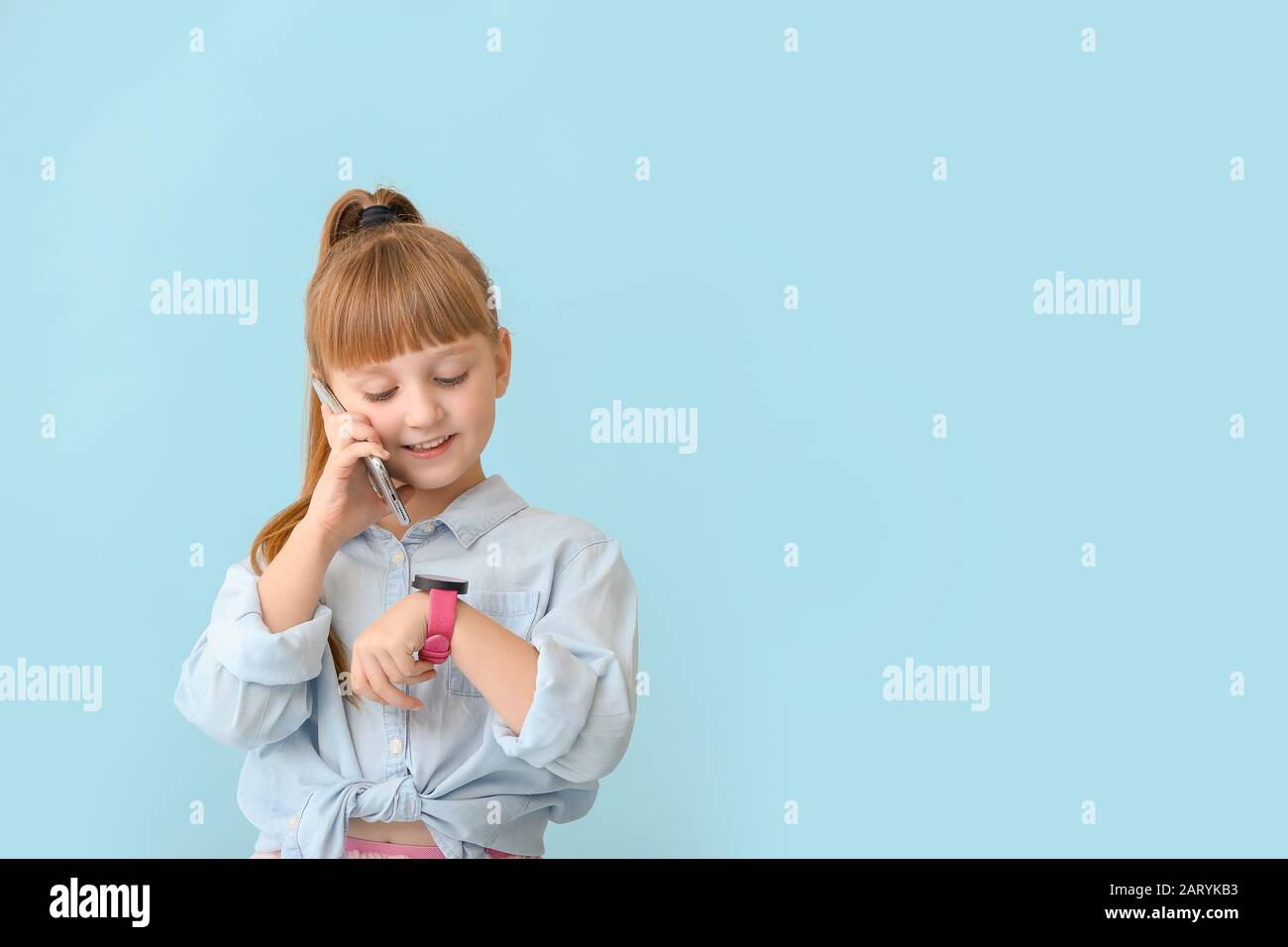 Cute little girl talking by phone while looking at watch on color ...