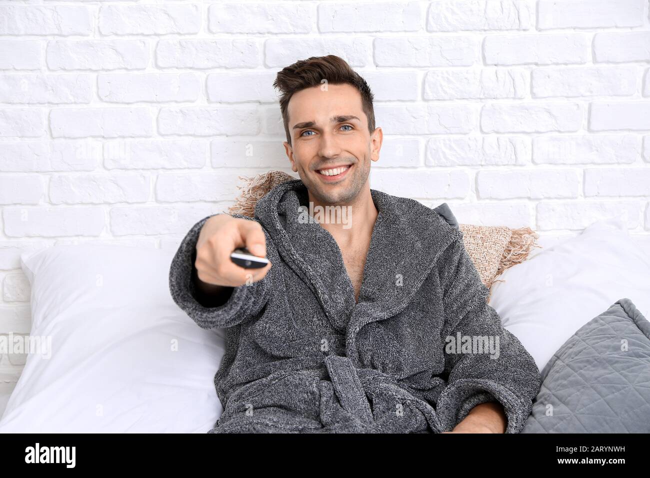 Handsome man in bathrobe watching TV on bed Stock Photo - Alamy