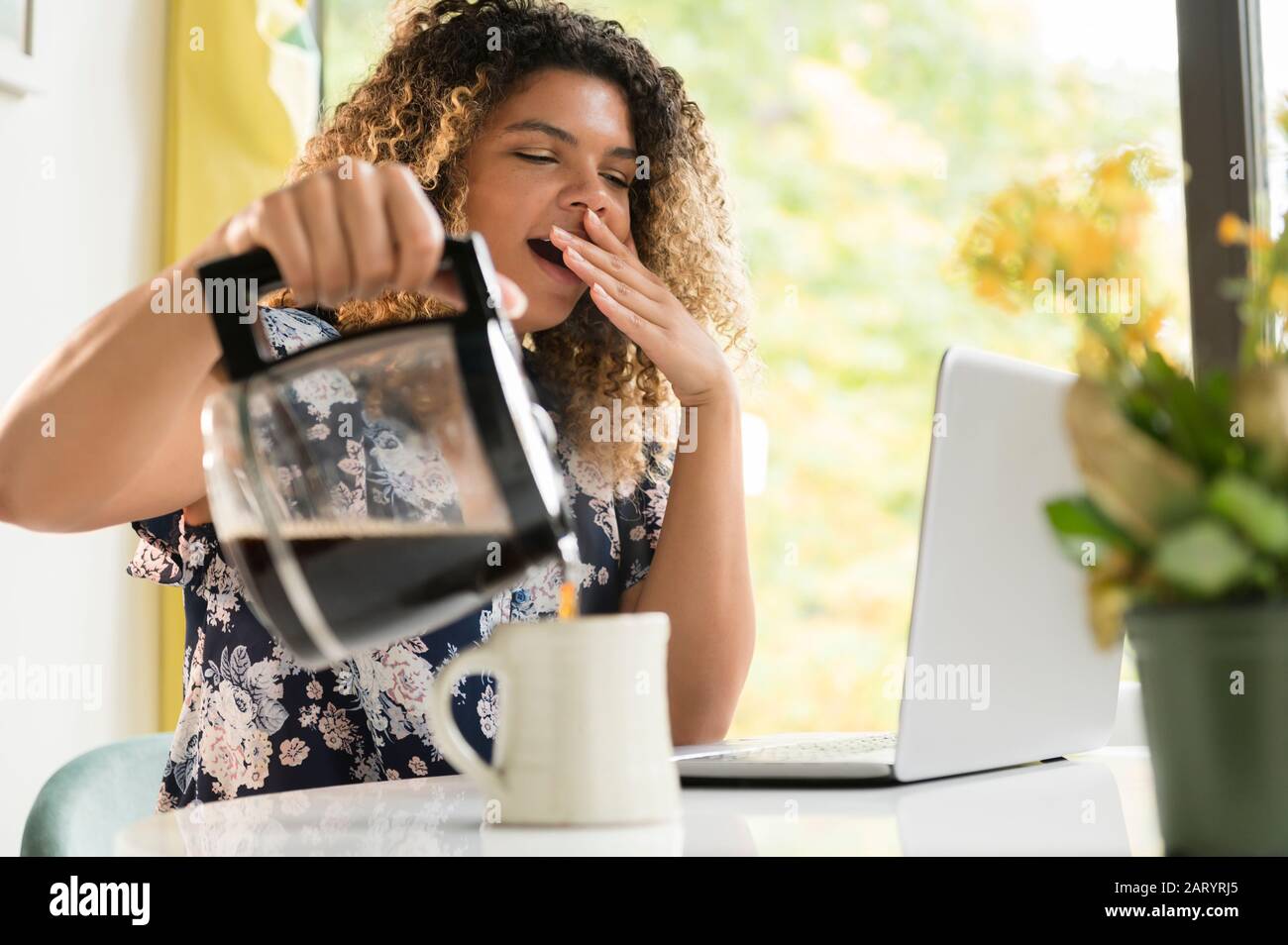 Tired woman pouring coffee by laptop Stock Photo - Alamy