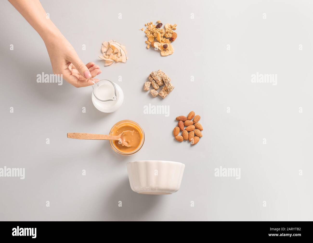 Female hand with jug of yogurt, tasty granola and ingredients on white ...