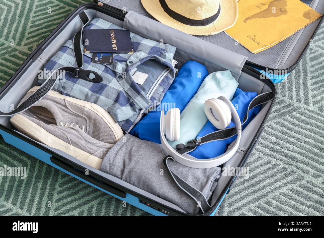 Open suitcase with packed clothes and accessories on floor at home ...