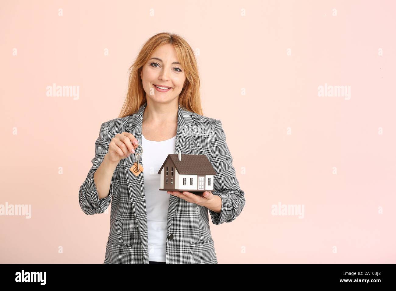Female real estate agent with key and model of house on color ...