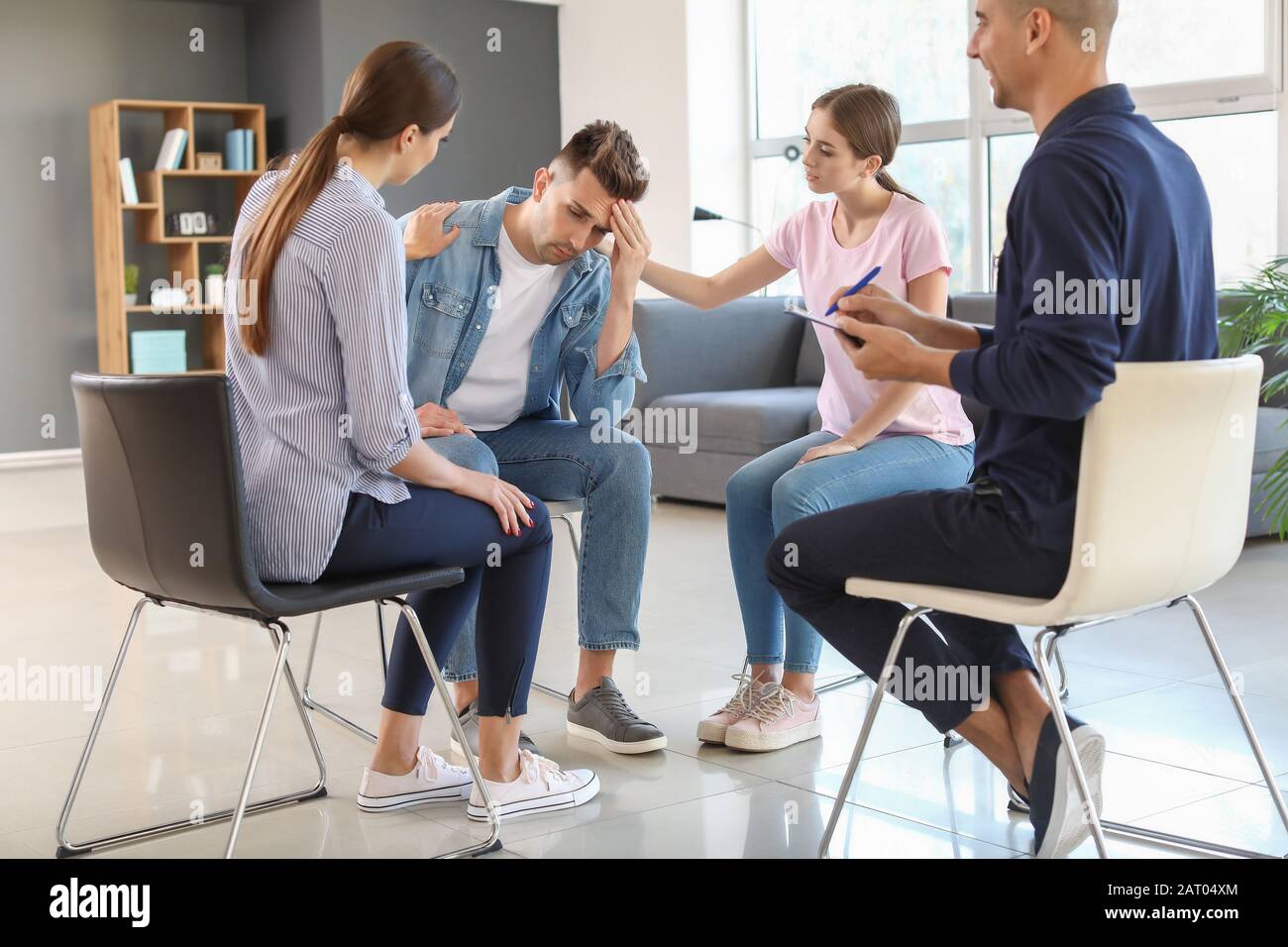 Young people calming sad man during psychological support session Stock ...