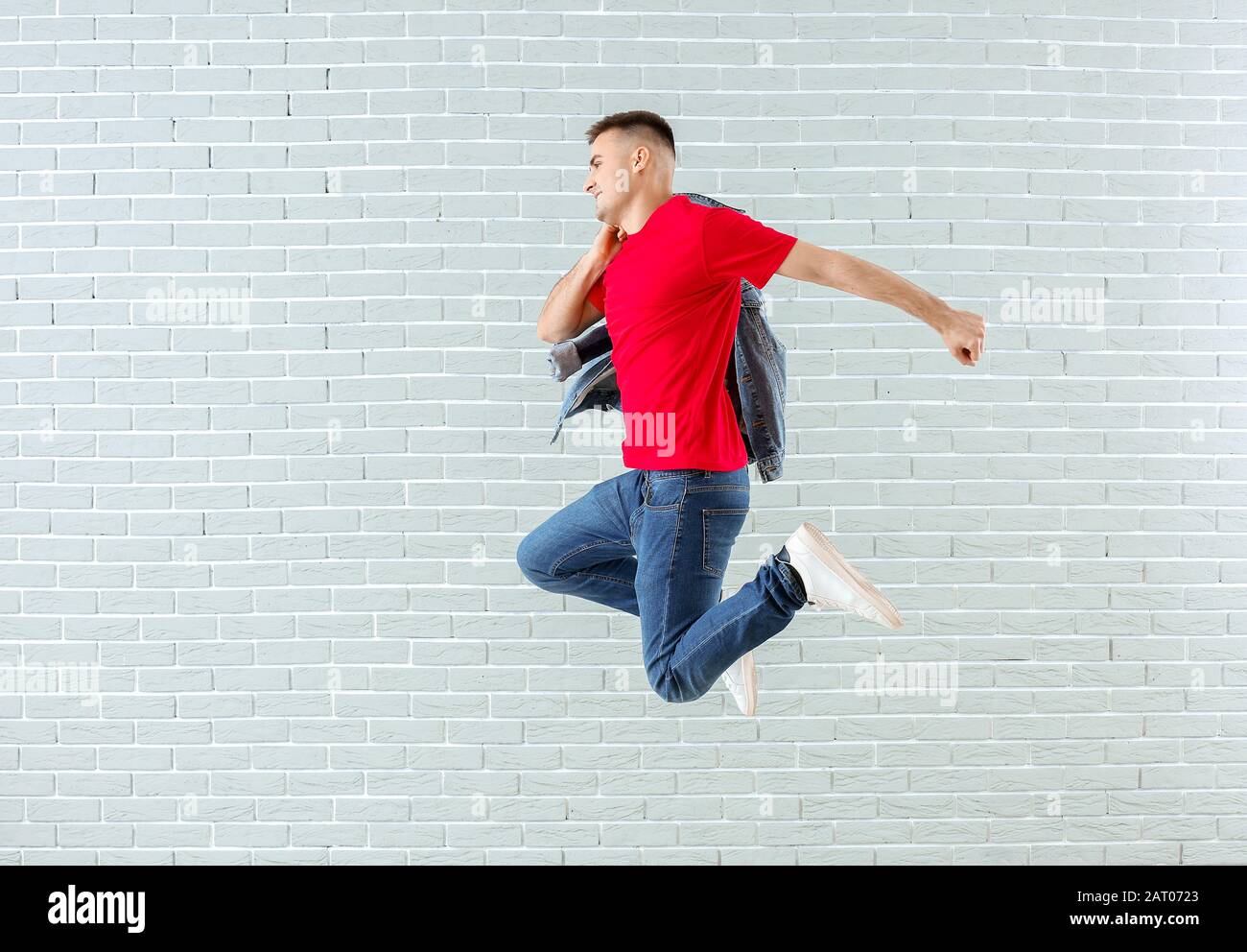 Jumping young man against brick wall Stock Photo - Alamy