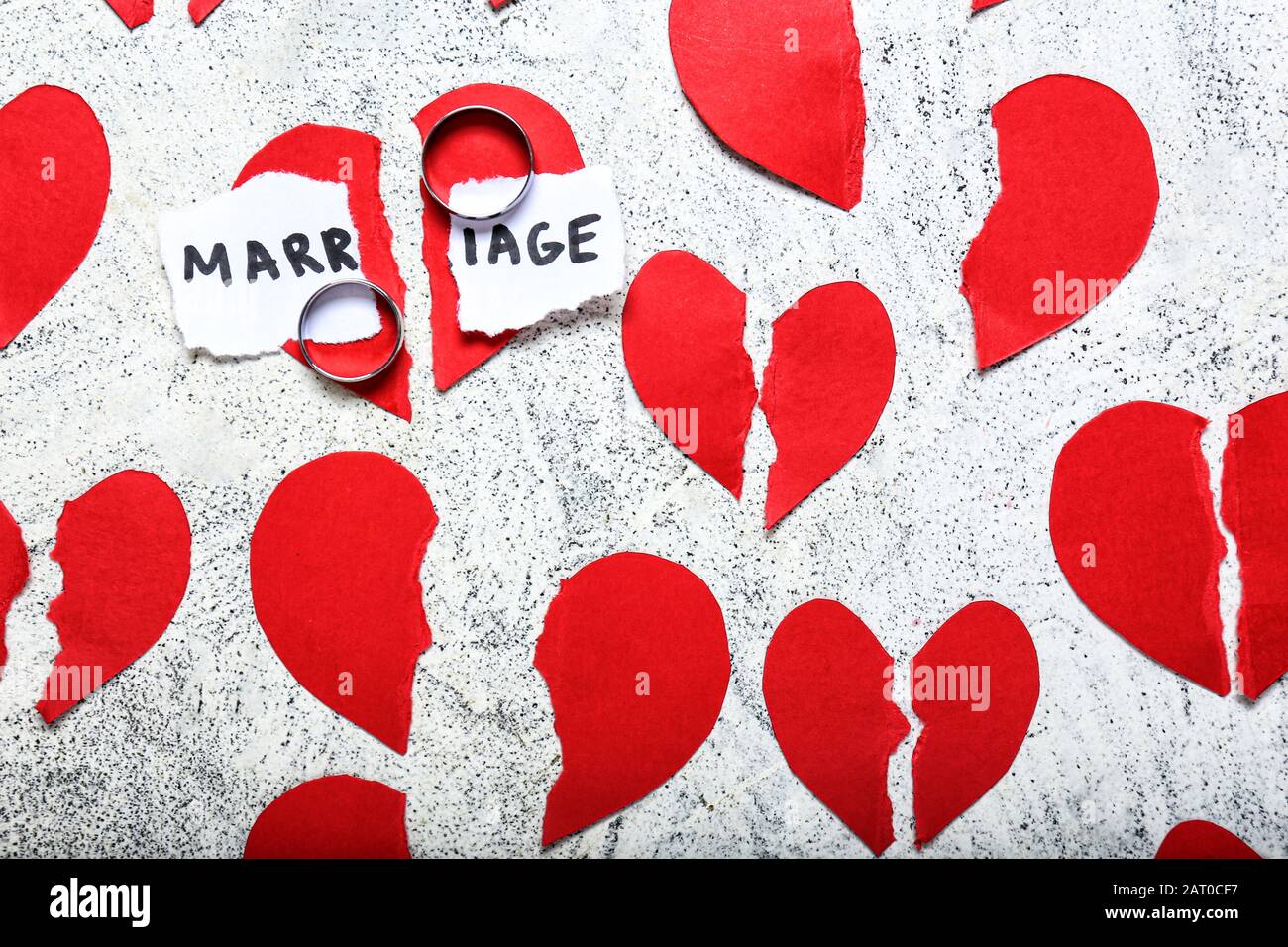 Many broken hearts, rings and torn paper with word MARRIAGE on light ...