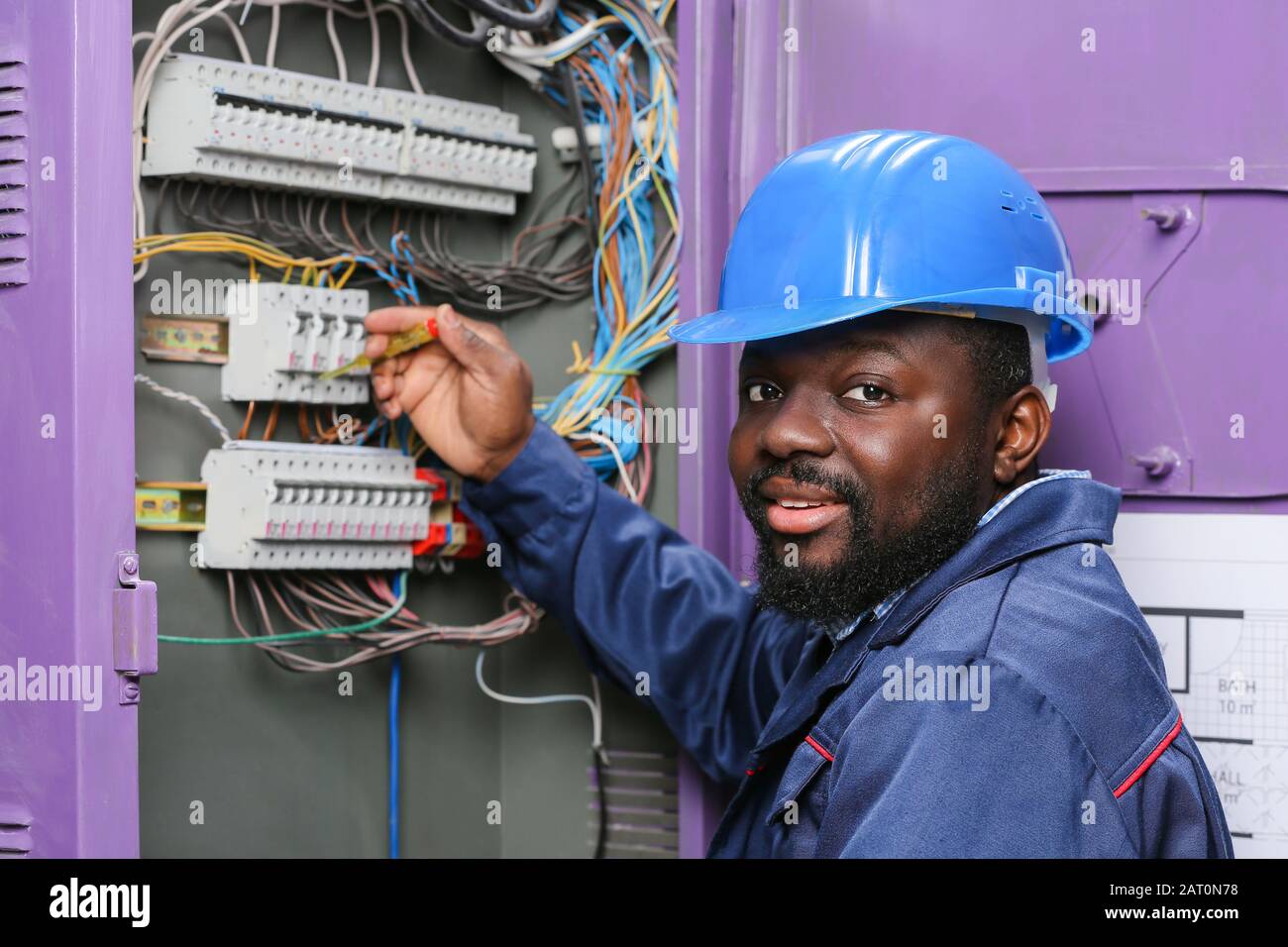 African-American electrician performing wiring in distribution board ...