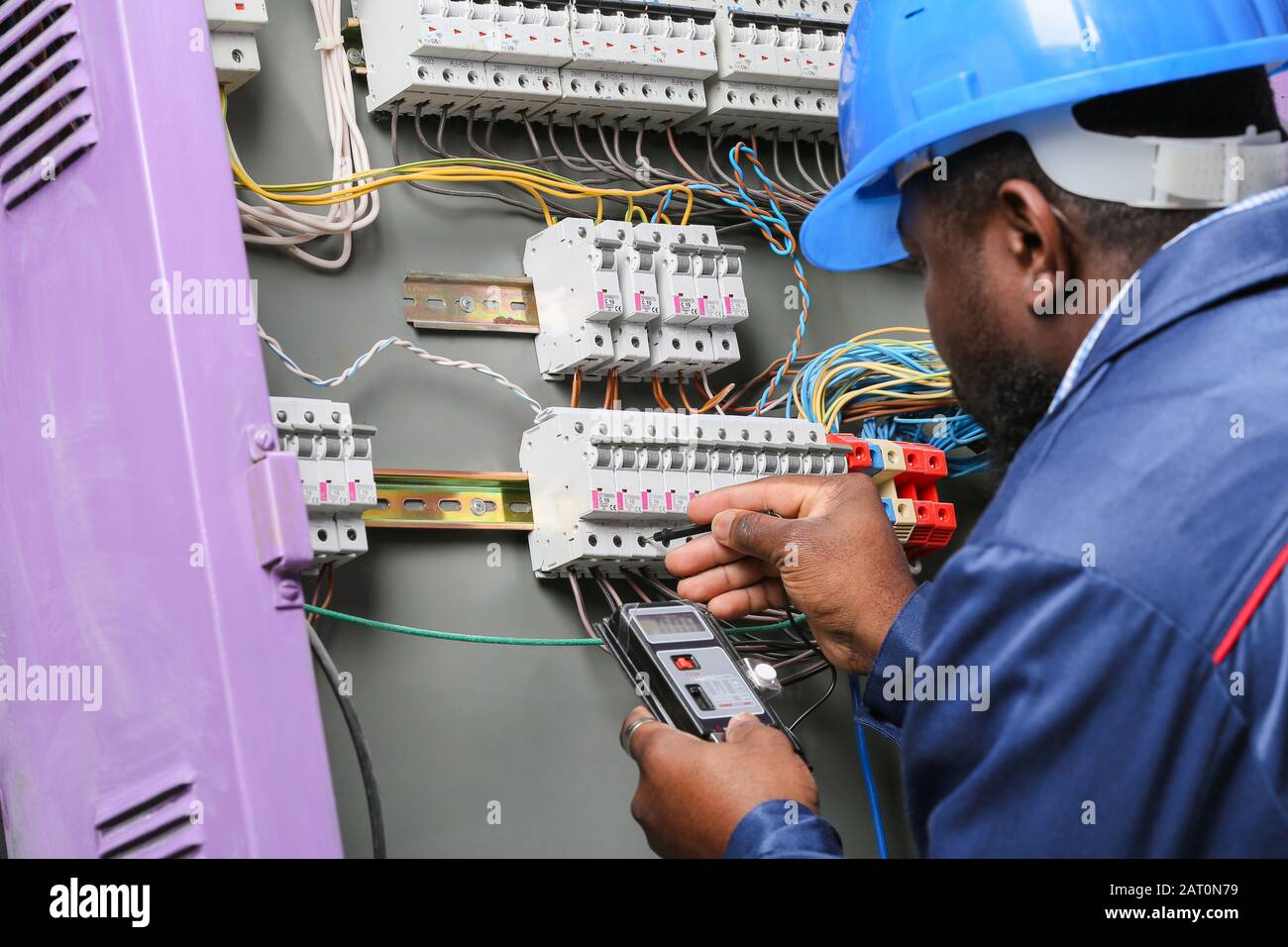 African-American electrician performing wiring in distribution board ...