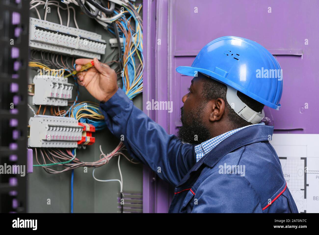 African-American electrician performing wiring in distribution board ...