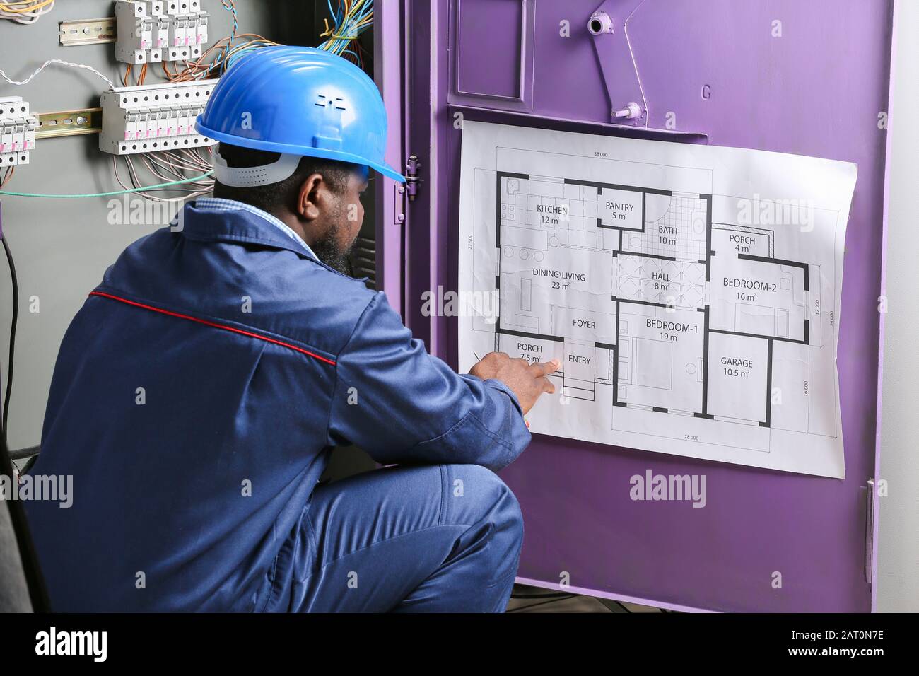African-American electrician performing wiring in distribution board ...