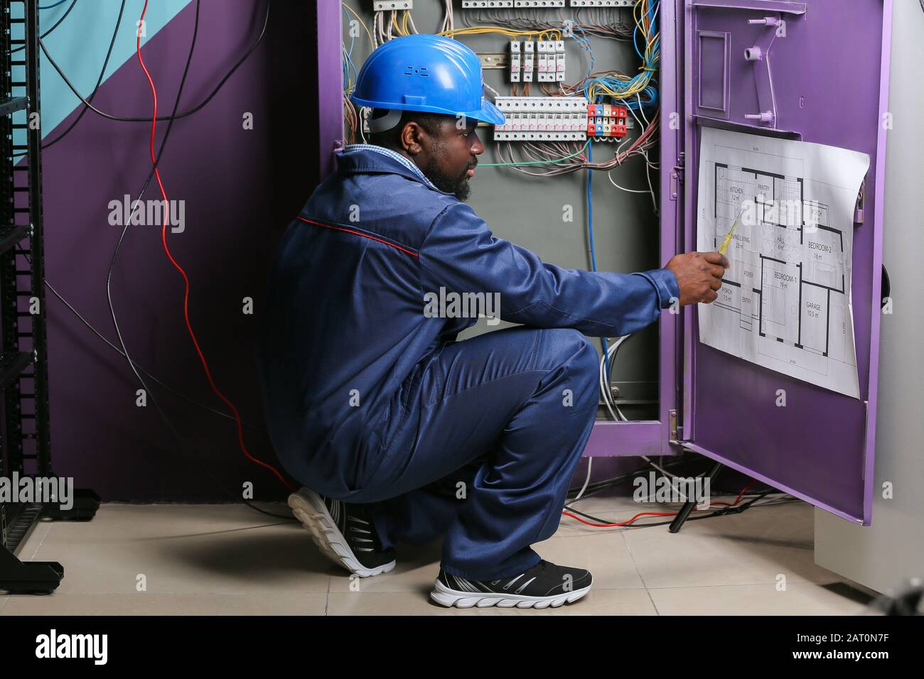 African-American electrician performing wiring in distribution board ...