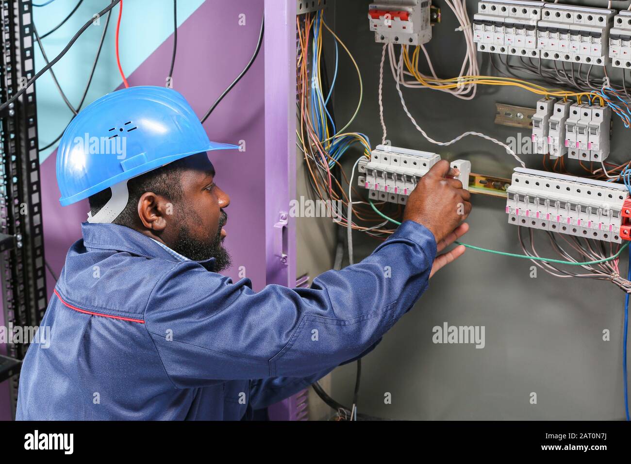 African-American electrician performing wiring in distribution board ...