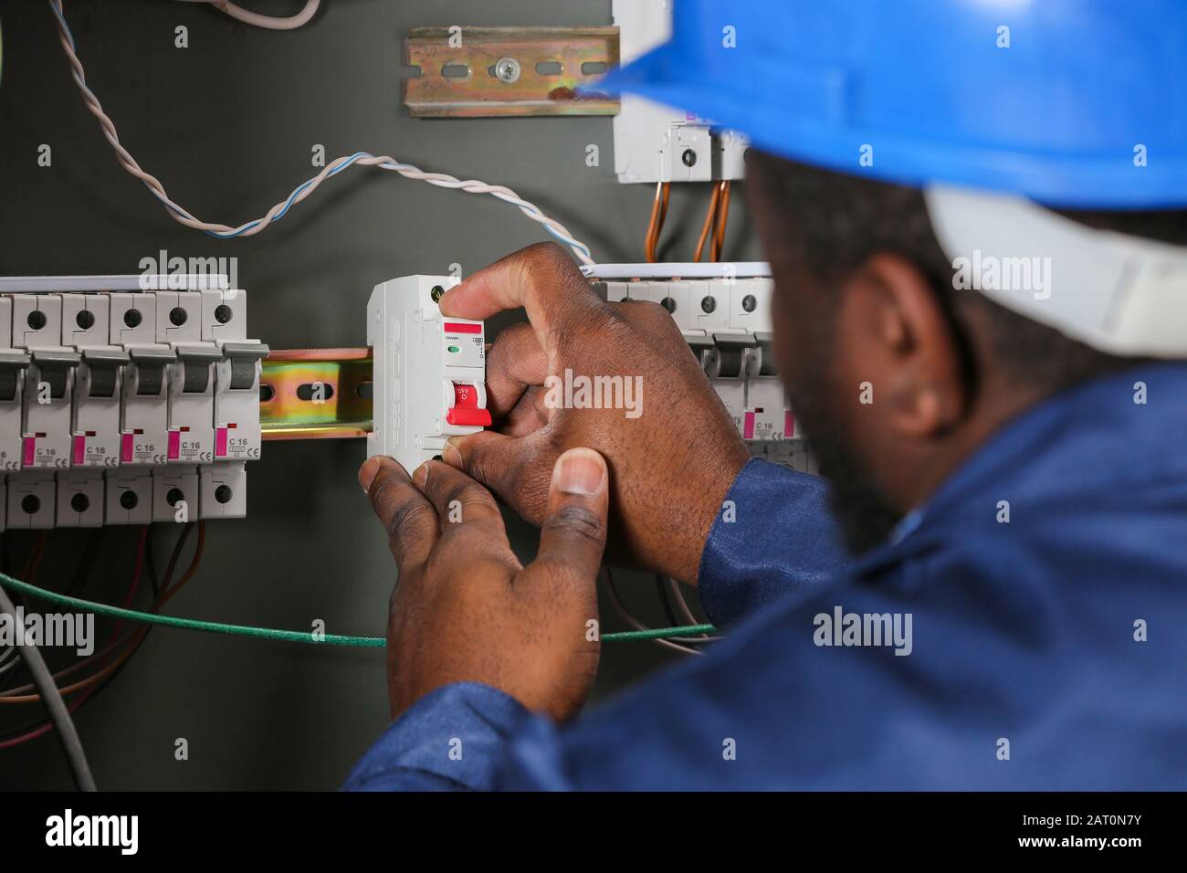 African-American electrician performing wiring in distribution board ...