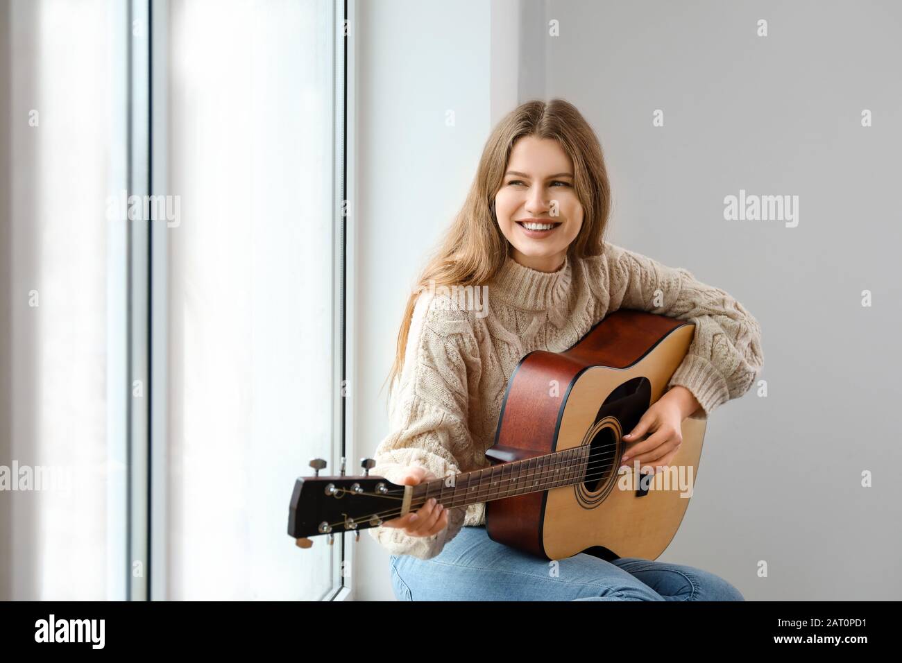 Young woman with guitar sitting on window sill at home Stock Photo - Alamy