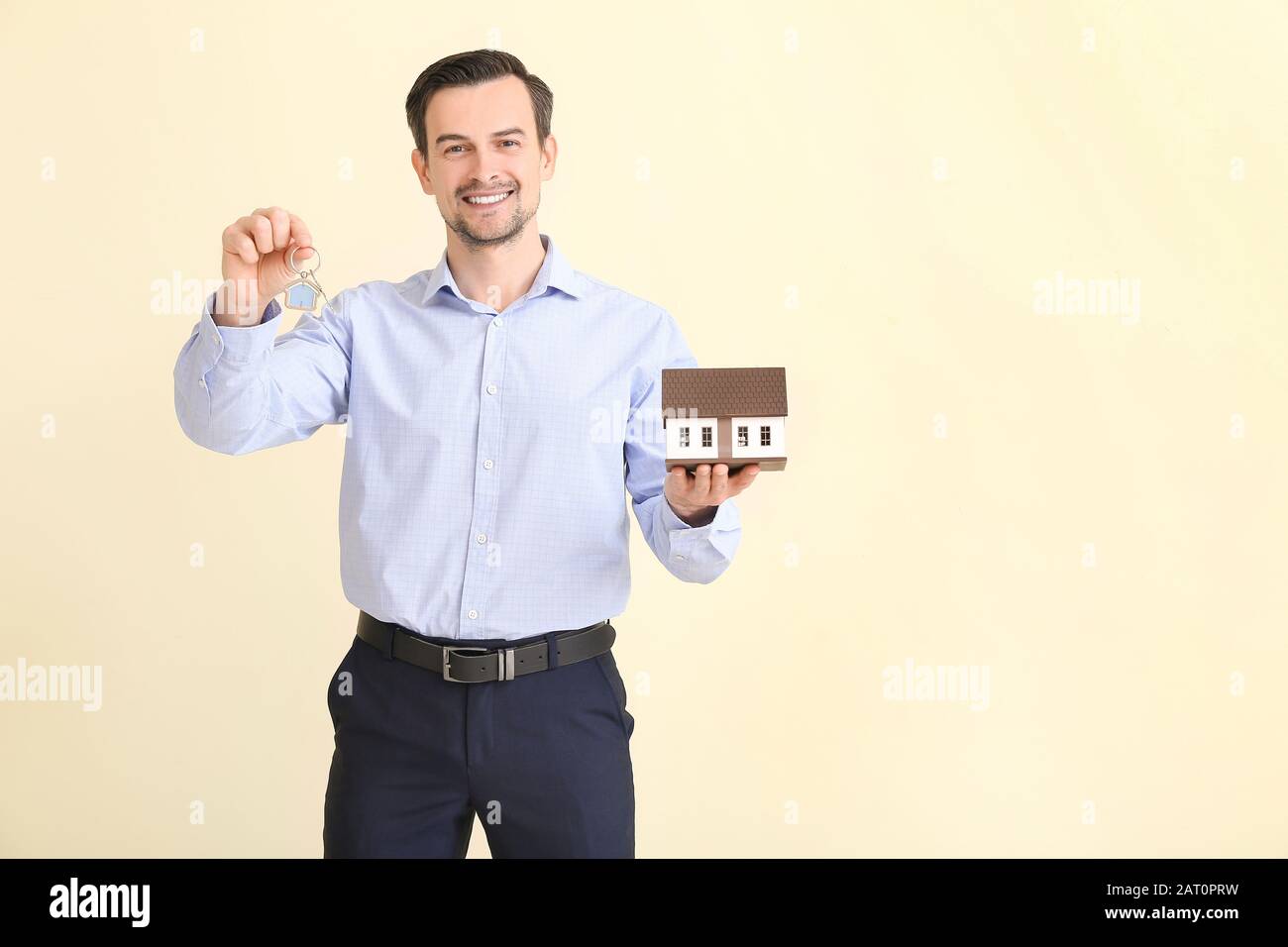 Male real estate agent with key and model of house on light background ...