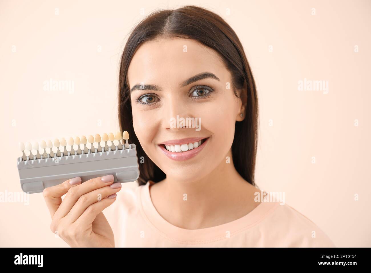 Beautiful young woman with teeth color samples on light background ...