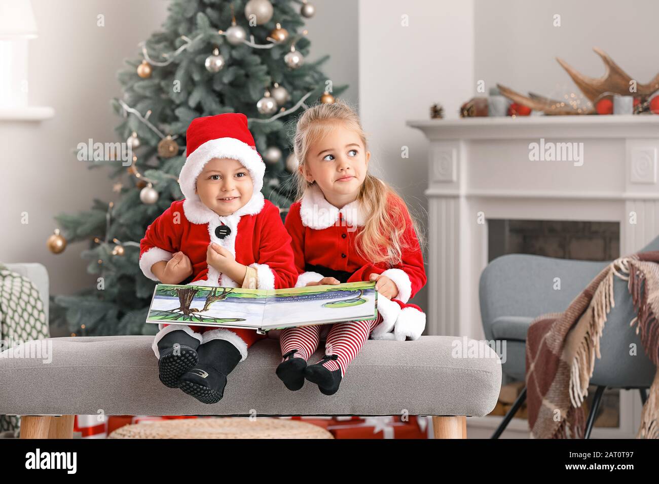 Cute little children in Santa costumes and with book at home on ...