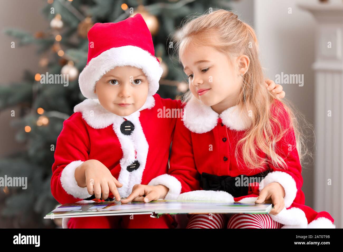 Cute little children in Santa costumes and with book at home on ...