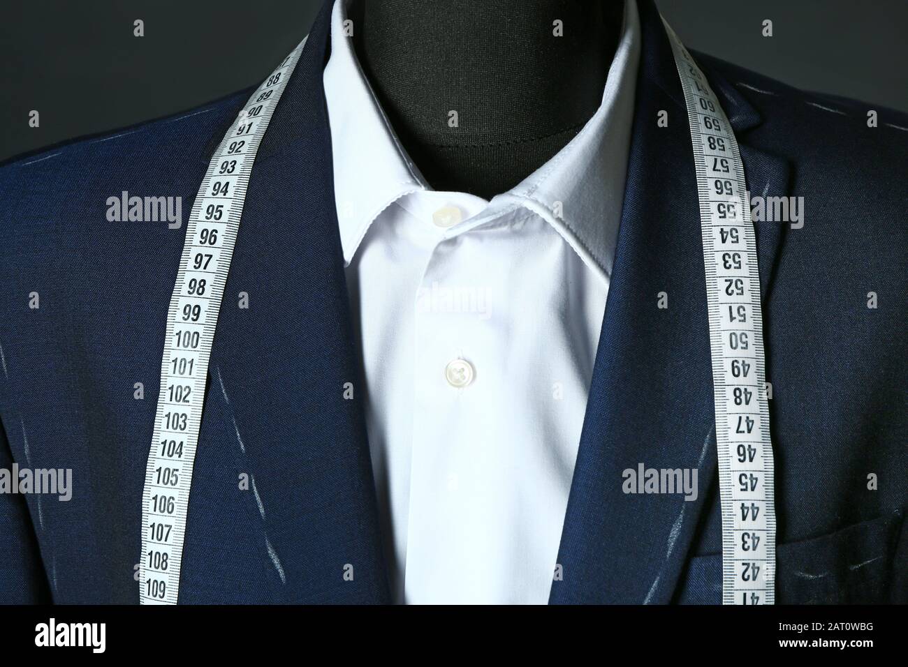 Tailor's mannequin with unfinished clothes and measuring tape on dark ...