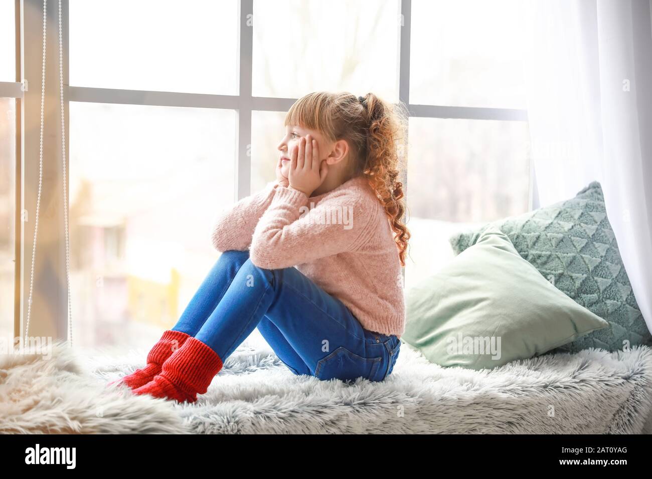 Cute little girl sitting on window sill at home Stock Photo - Alamy