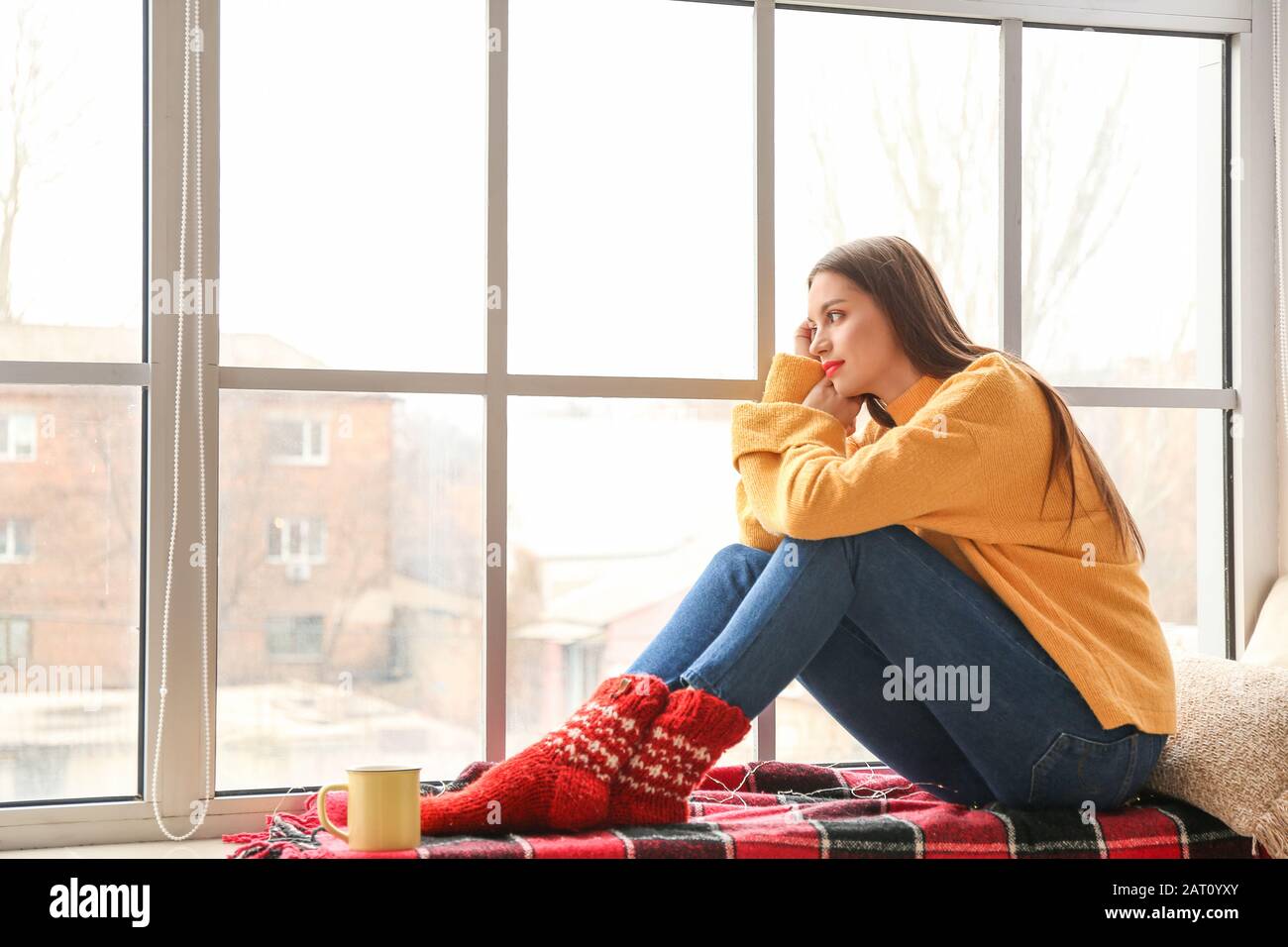 Young woman in winter clothes sitting on window sill at home Stock ...