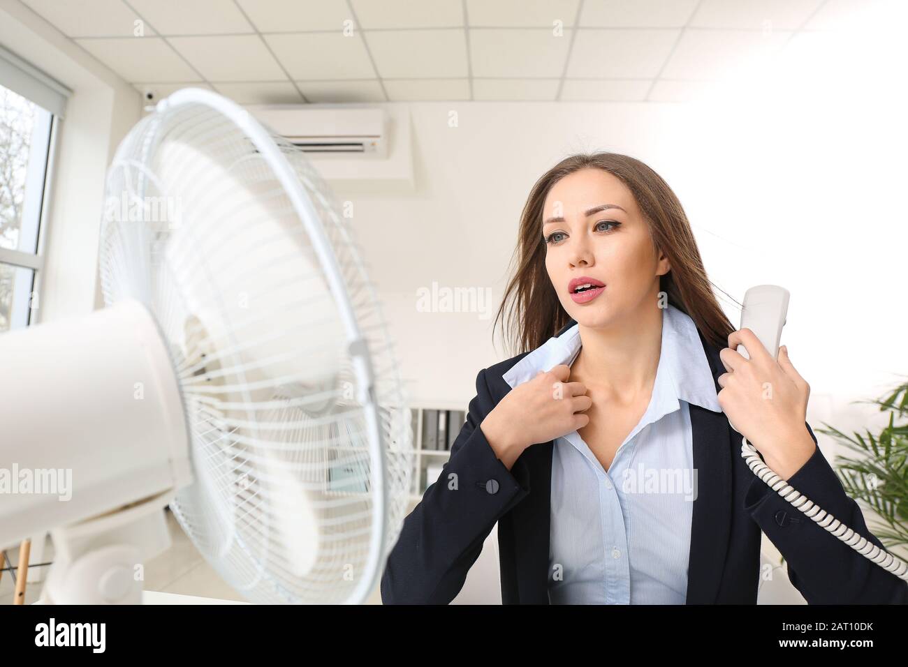 Young woman using electric fan during heatwave in office Stock Photo ...