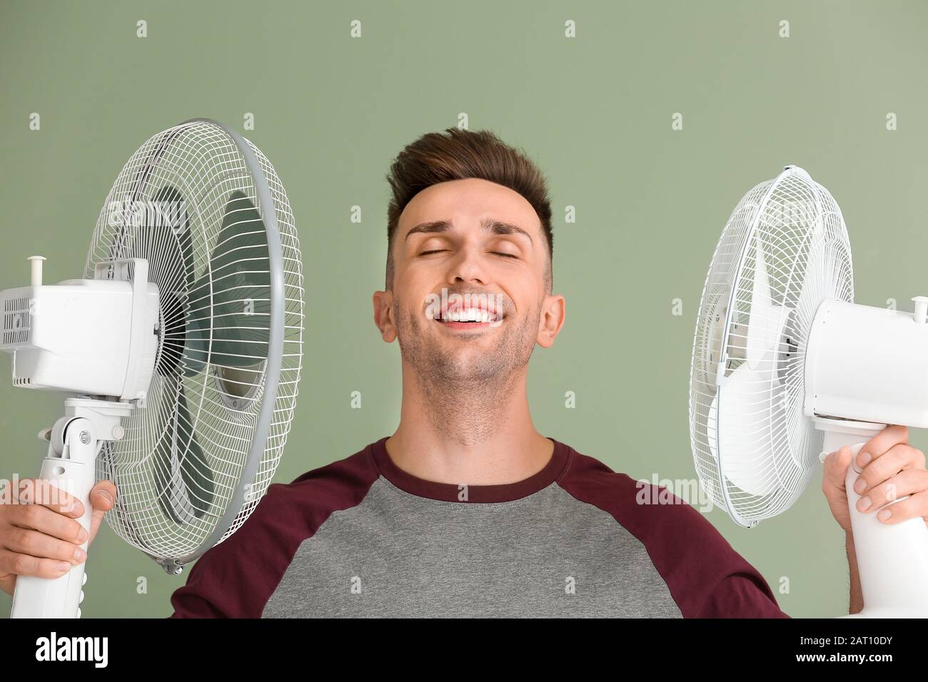 Young man with electric fans on color background Stock Photo - Alamy