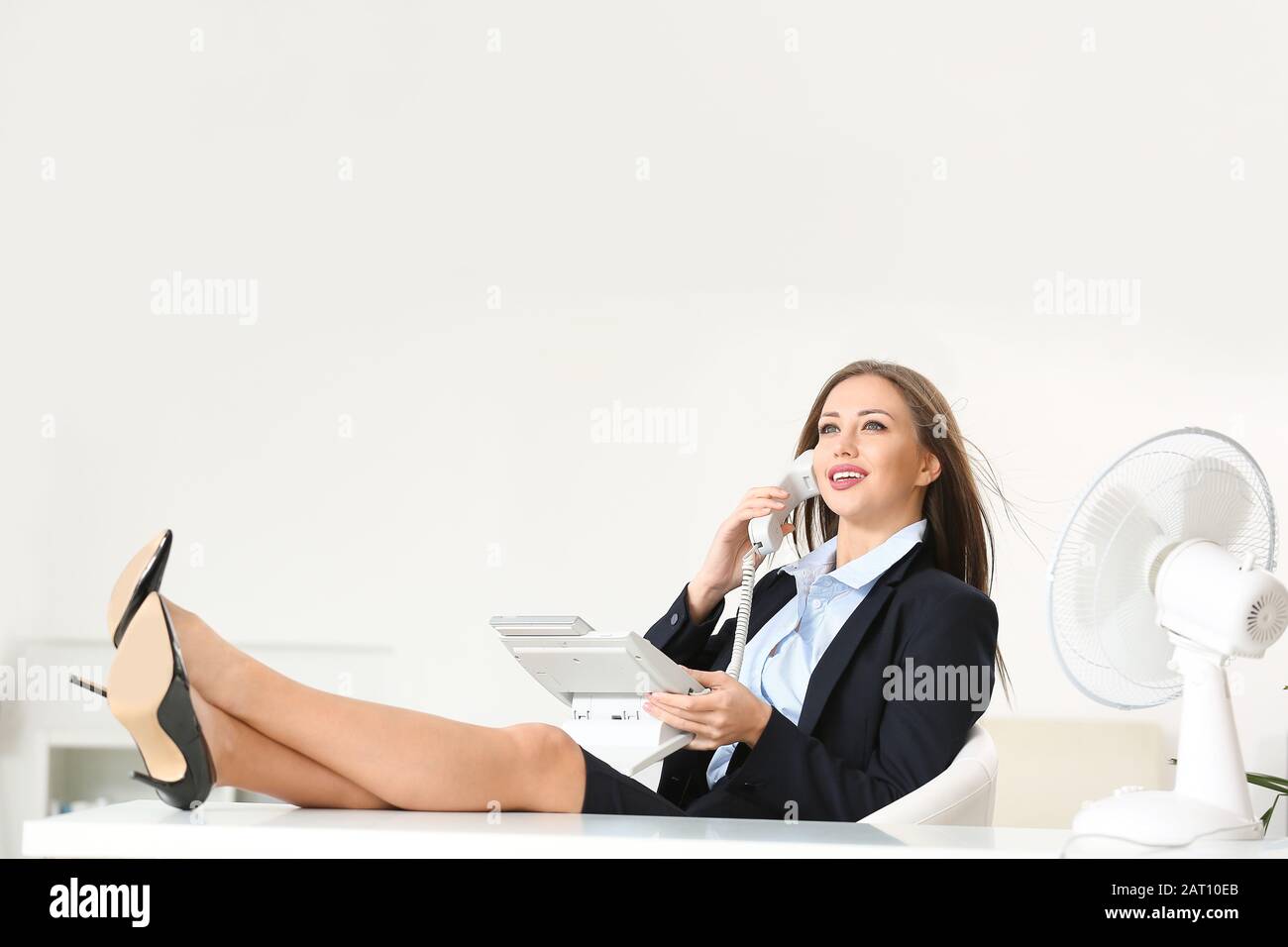 Young woman using electric fan during heatwave in office Stock Photo ...