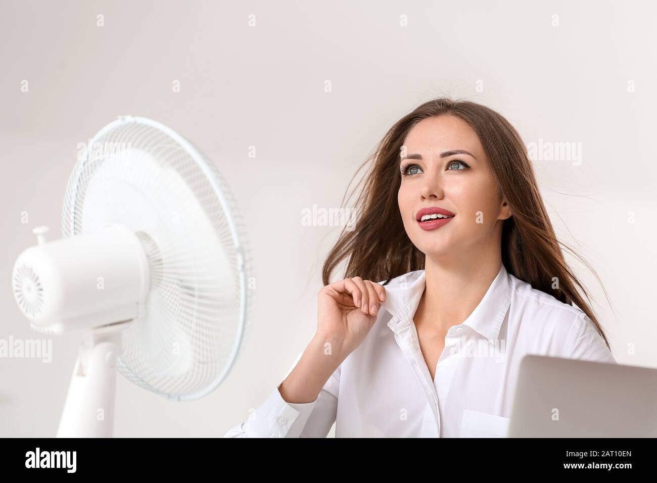 Young woman using electric fan during heatwave in office Stock Photo ...