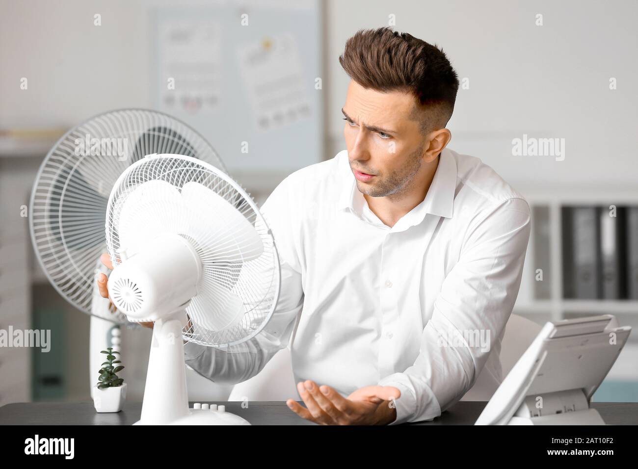 Confused man suffering from heat near electric fan in office Stock ...