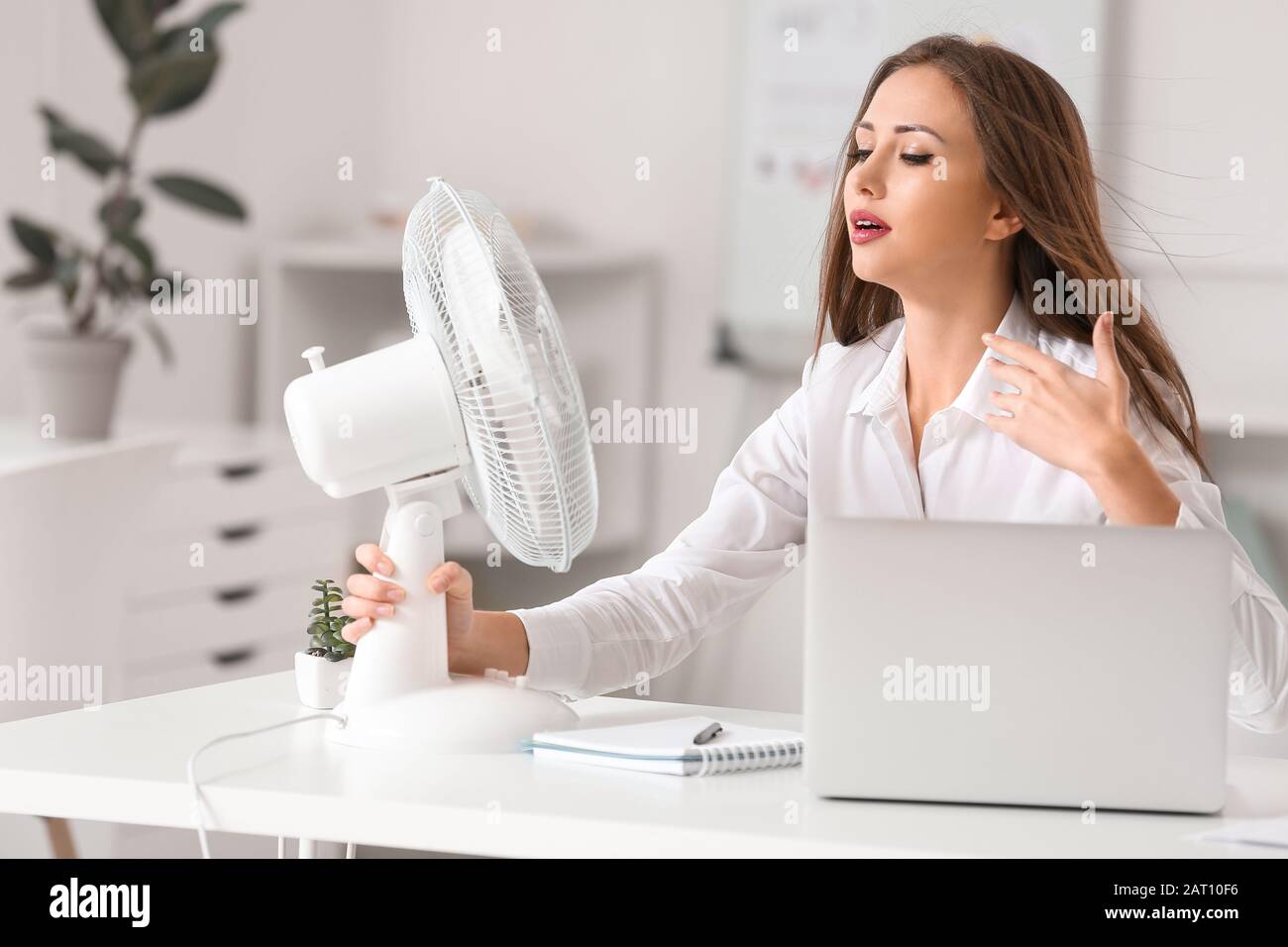 Young woman using electric fan during heatwave in office Stock Photo ...