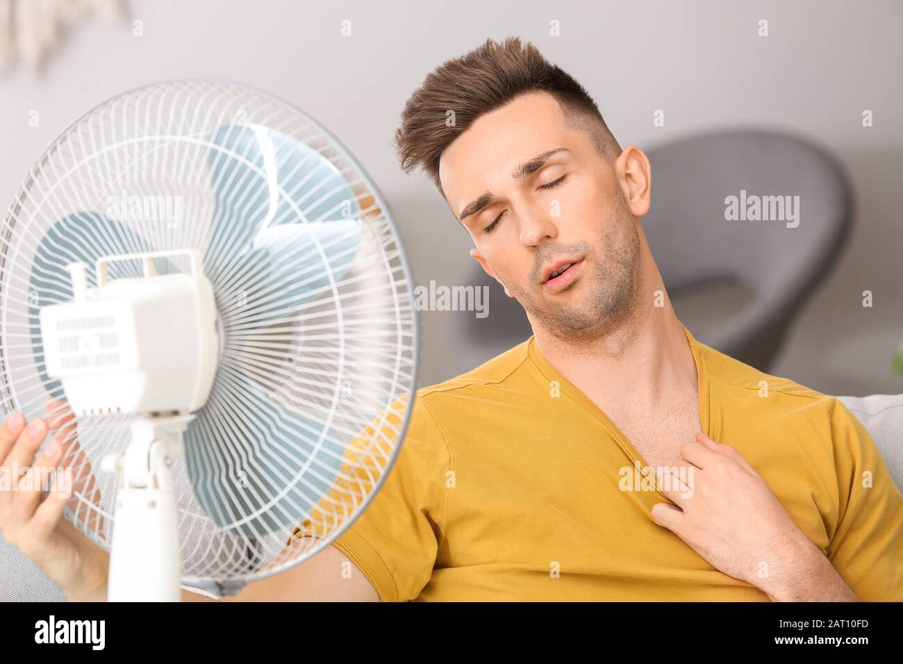 Young man using electric fan during heatwave at home Stock Photo - Alamy
